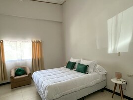 Quarto com uma cama grande, uma cadeira, uma mesa pequena e uma janela com cortinas.