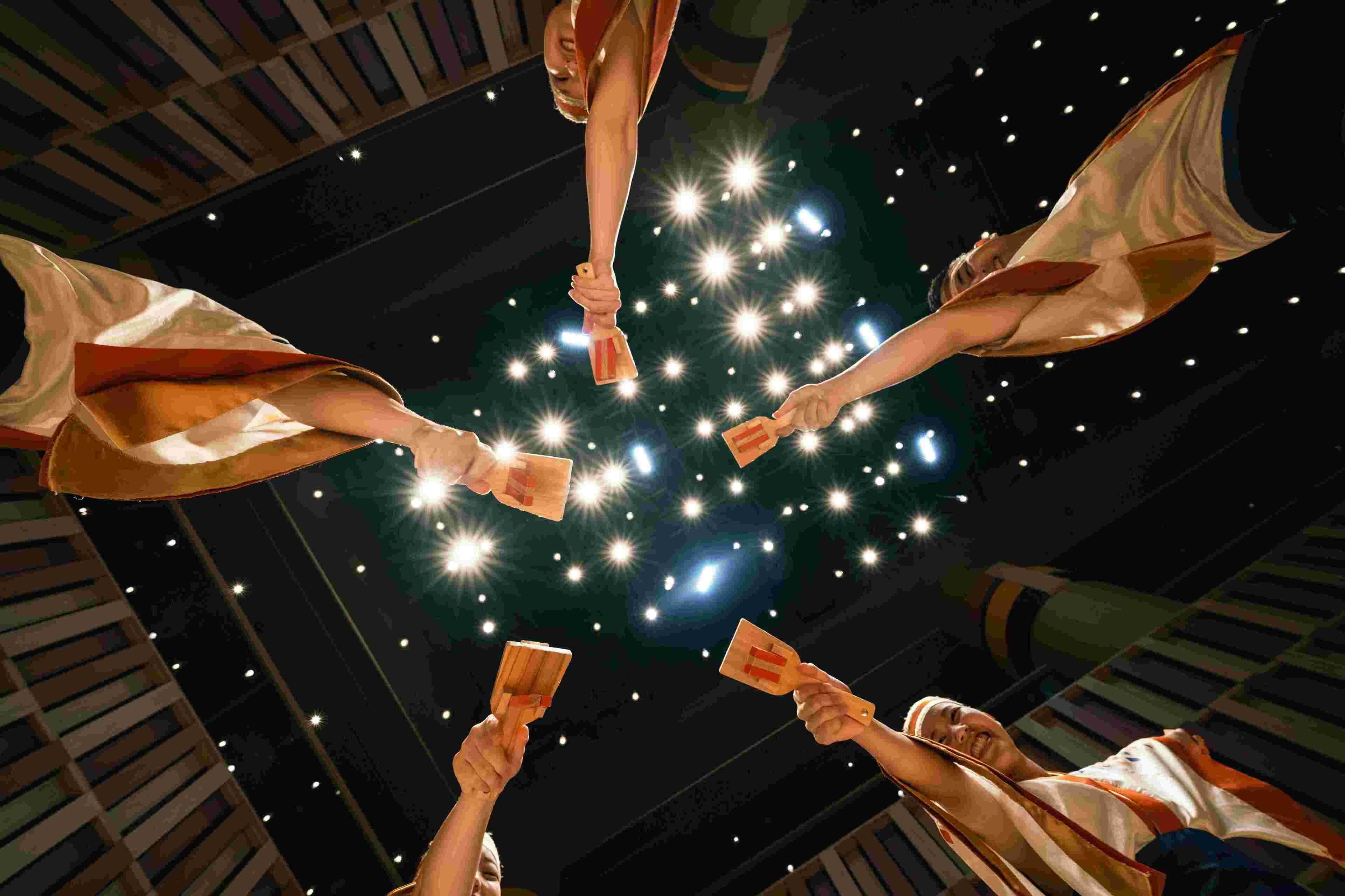 Um grupo de pessoas de mãos dadas formando um círculo, com uma luz intensa acima.