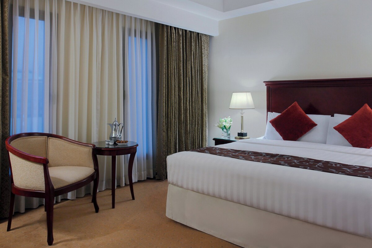 Quarto de hotel com cama, cadeira, mesa de cabeceira e abajur.