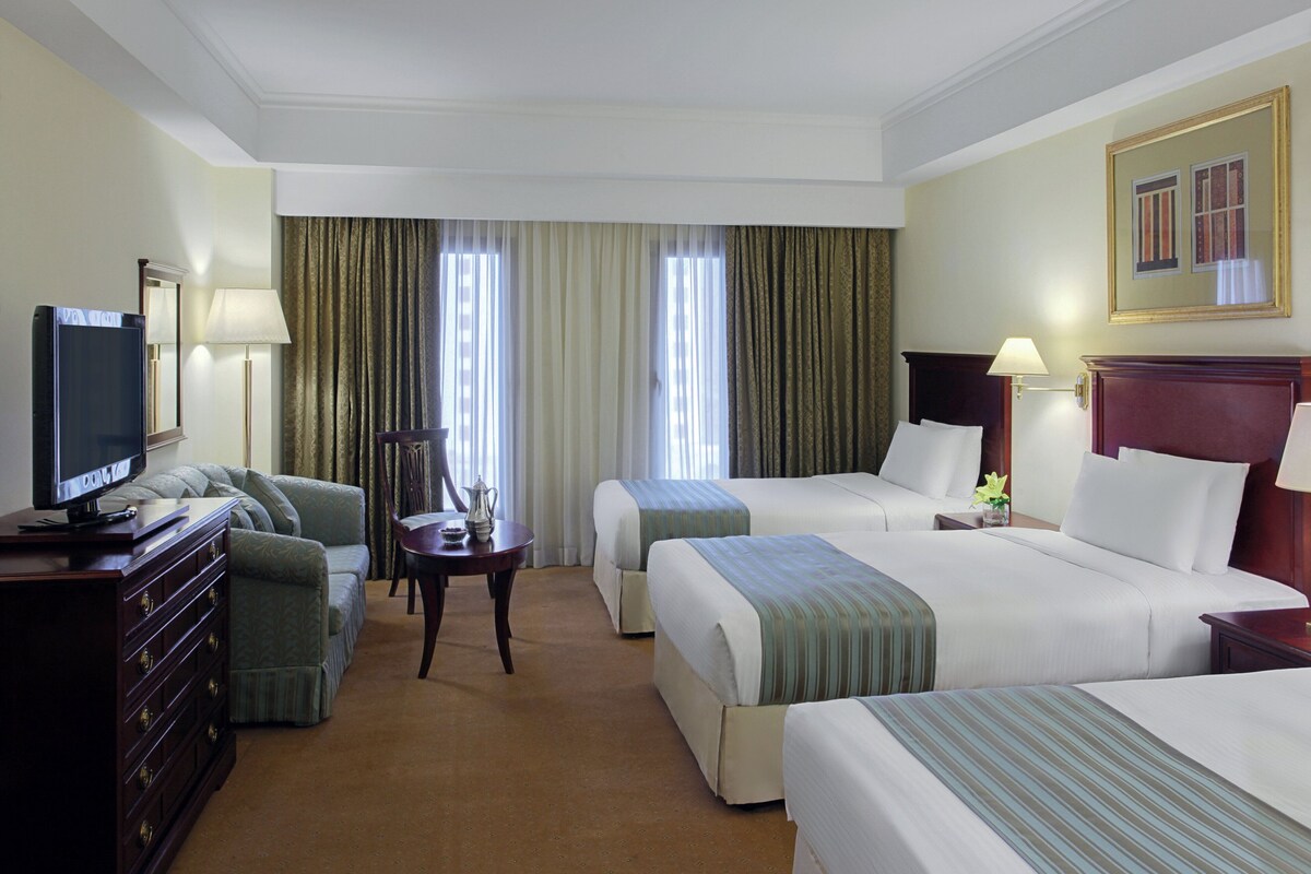 Quarto de hotel com duas camas, televisão, cômoda e escrivaninha com luminária.
