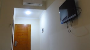 Quarto com porta de madeira, TV de tela plana montada e ar condicionado na parede.