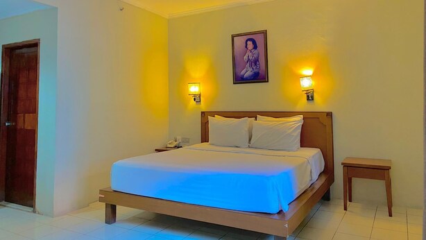 Quarto de hotel com cama, mesas de cabeceira e luminárias fixadas na parede.