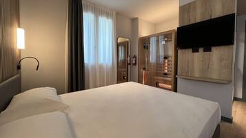 Quarto de hotel com uma cama grande, luminária, espelho, guarda-roupa e televisão fixada na parede.