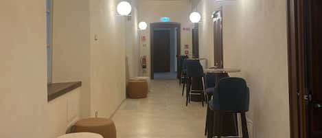 Um corredor com teto alto, iluminação embutida e vários espaços de estar com pufes e cadeiras.