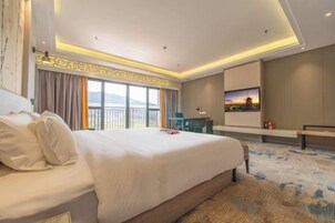 Quarto de hotel com uma cama grande, escrivaninha, cadeira, televisão e varanda com vista.