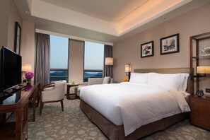 Quarto de hotel com uma cama grande, uma escrivaninha com uma TV, uma cadeira e vista para as montanhas pelas janelas.