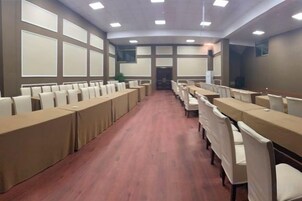 Uma sala de conferências com mesas compridas e cadeiras, piso de madeira e uma TV de tela plana fixada na parede.