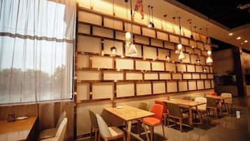 Um restaurante com várias mesas e cadeiras, uma parede com prateleiras e luminárias pendentes.
