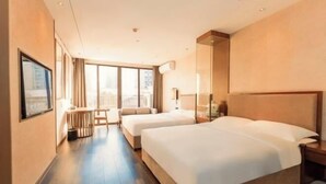 Quarto de hotel com duas camas, uma mesa pequena e uma janela grande.