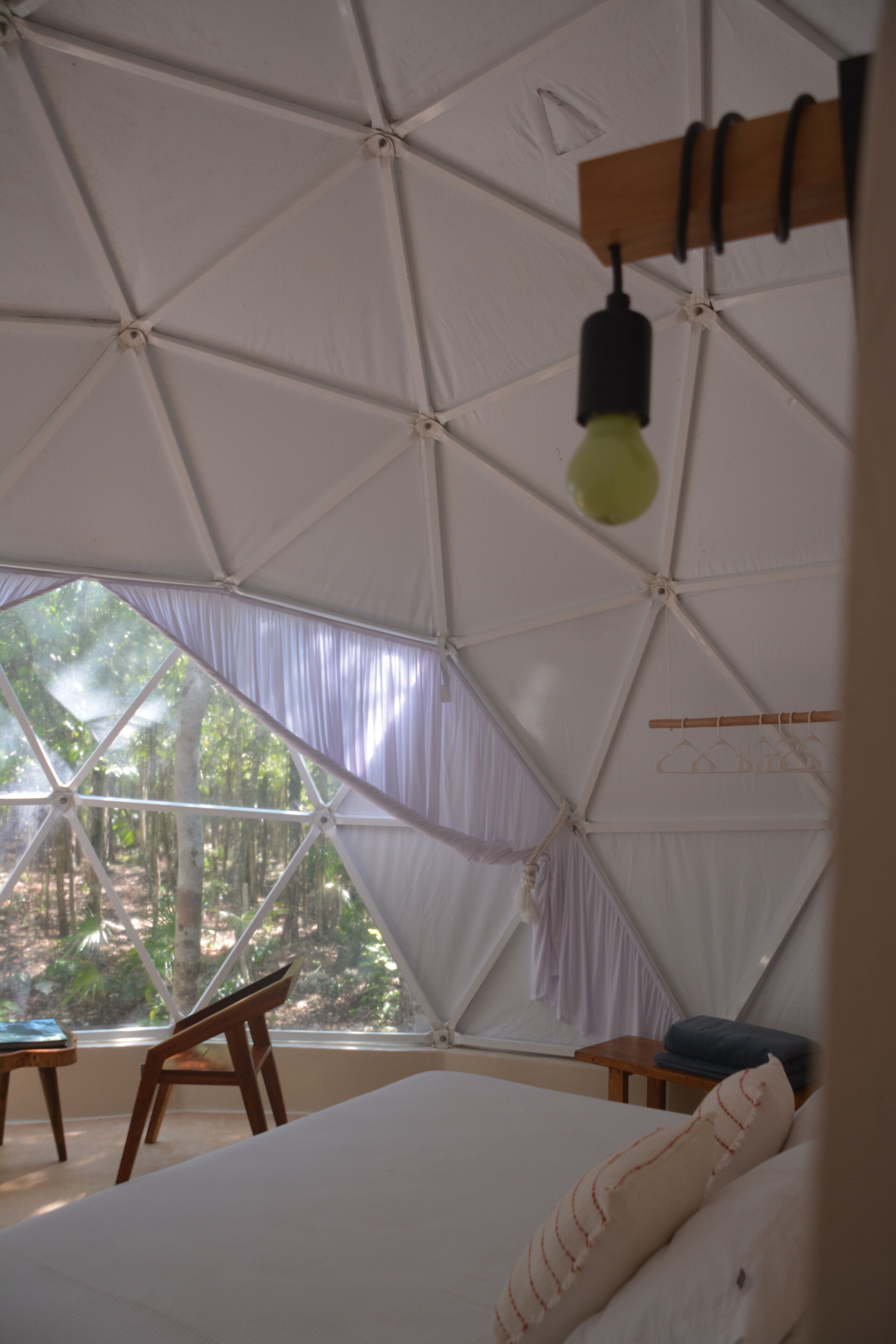 Um quarto com tenda, com uma cama, uma cadeira e um lustre pendurado.