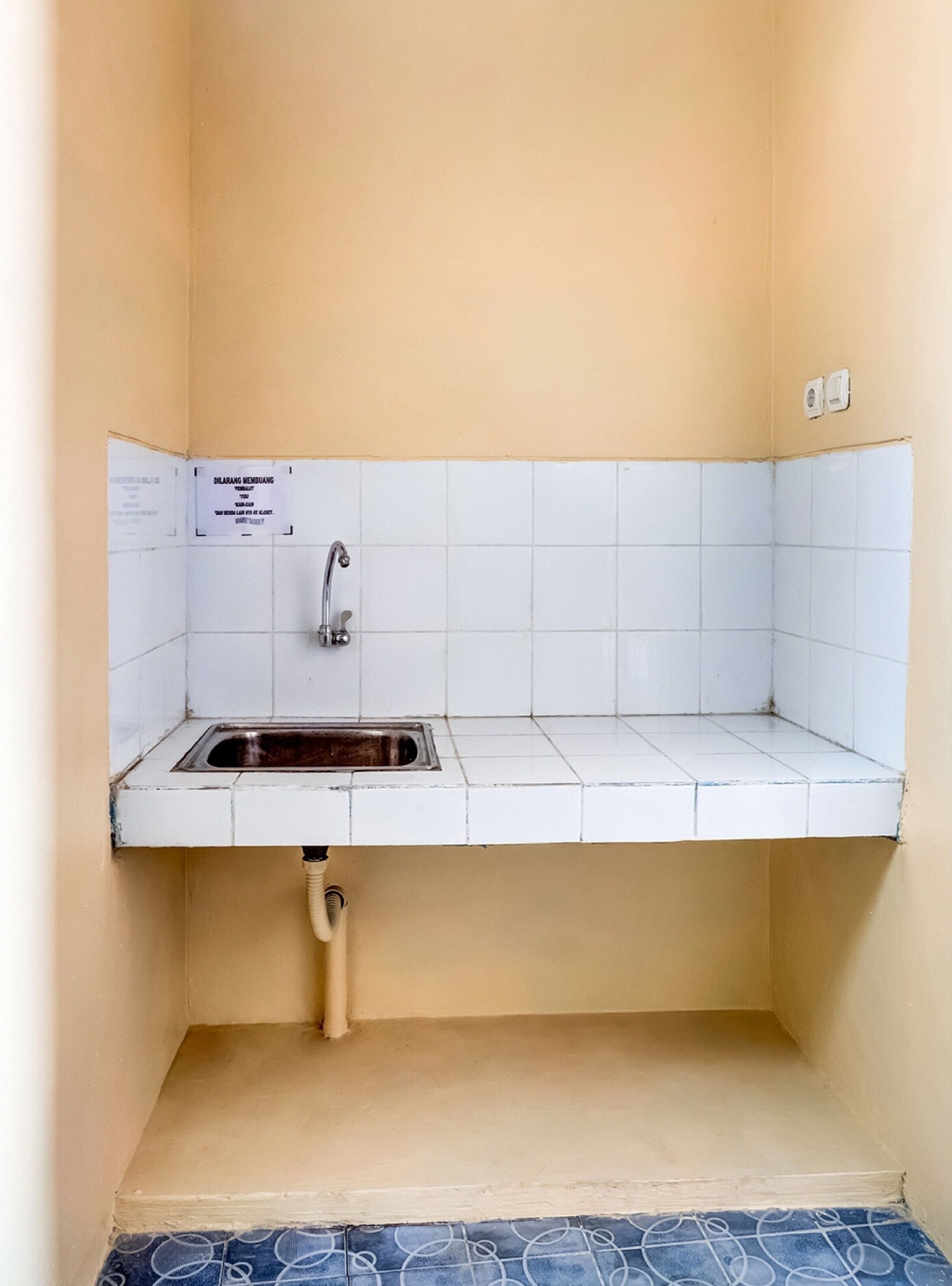 Casa de banho pequena e fechada, com lavatório, azulejos brancos e parede bege.