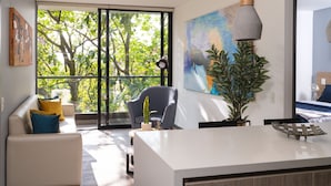 Uma sala de estar moderna com um sofá branco, uma poltrona cinzenta e uma janela grande com vista para árvores.
