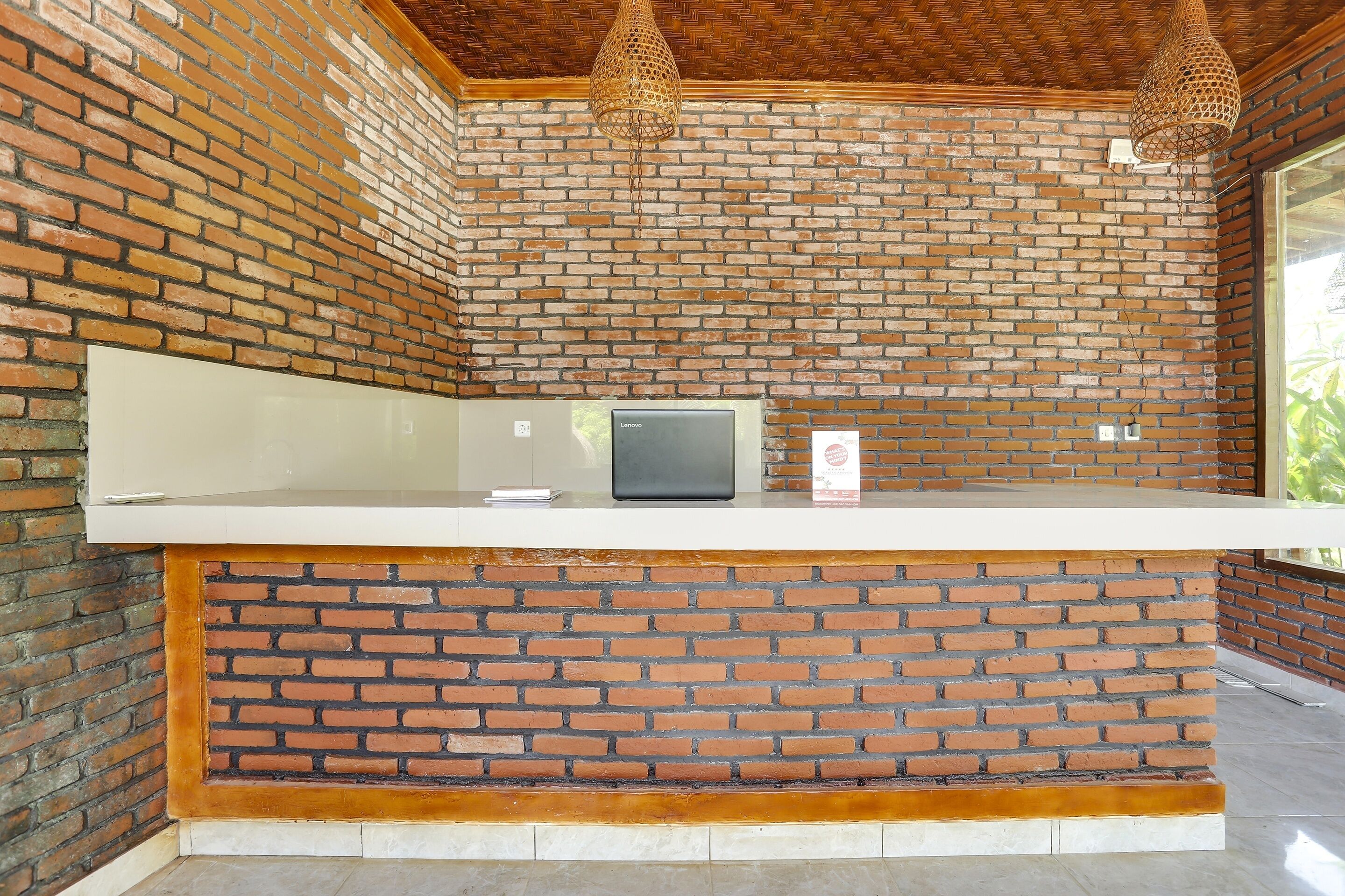 Bancada de recepção com parede de tijolos, um laptop e uma placa.