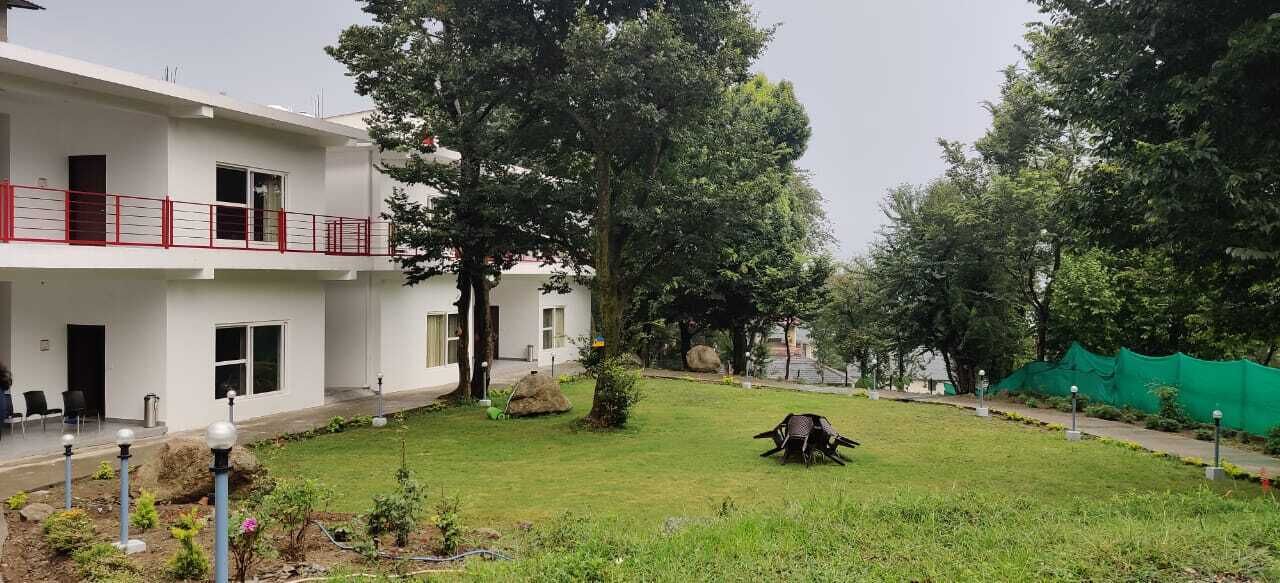 Um edifício com fachada branca, guarda-corpo de varanda vermelho e um gramado bem cuidado, com uma grande árvore e um comedouro para pássaros.