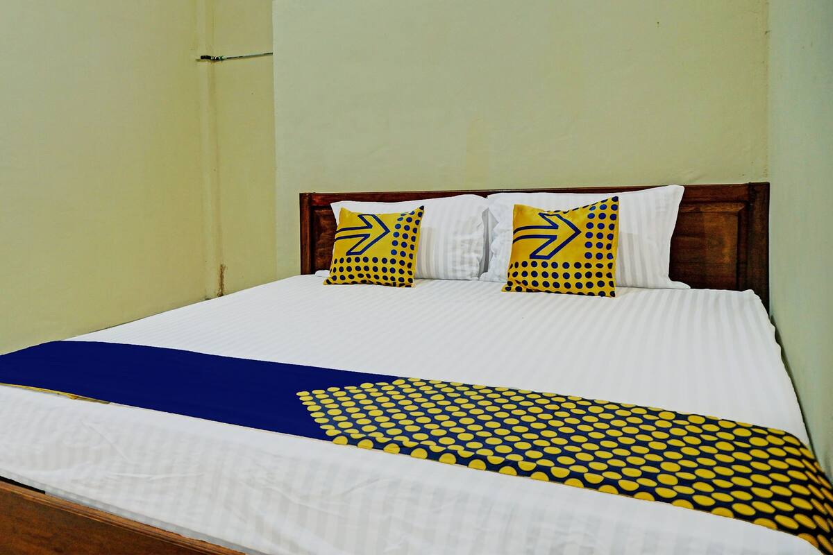 Uma cama com colcha branca e azul, duas almofadas com estampas amarelas e pretas, e uma cabeceira de madeira.