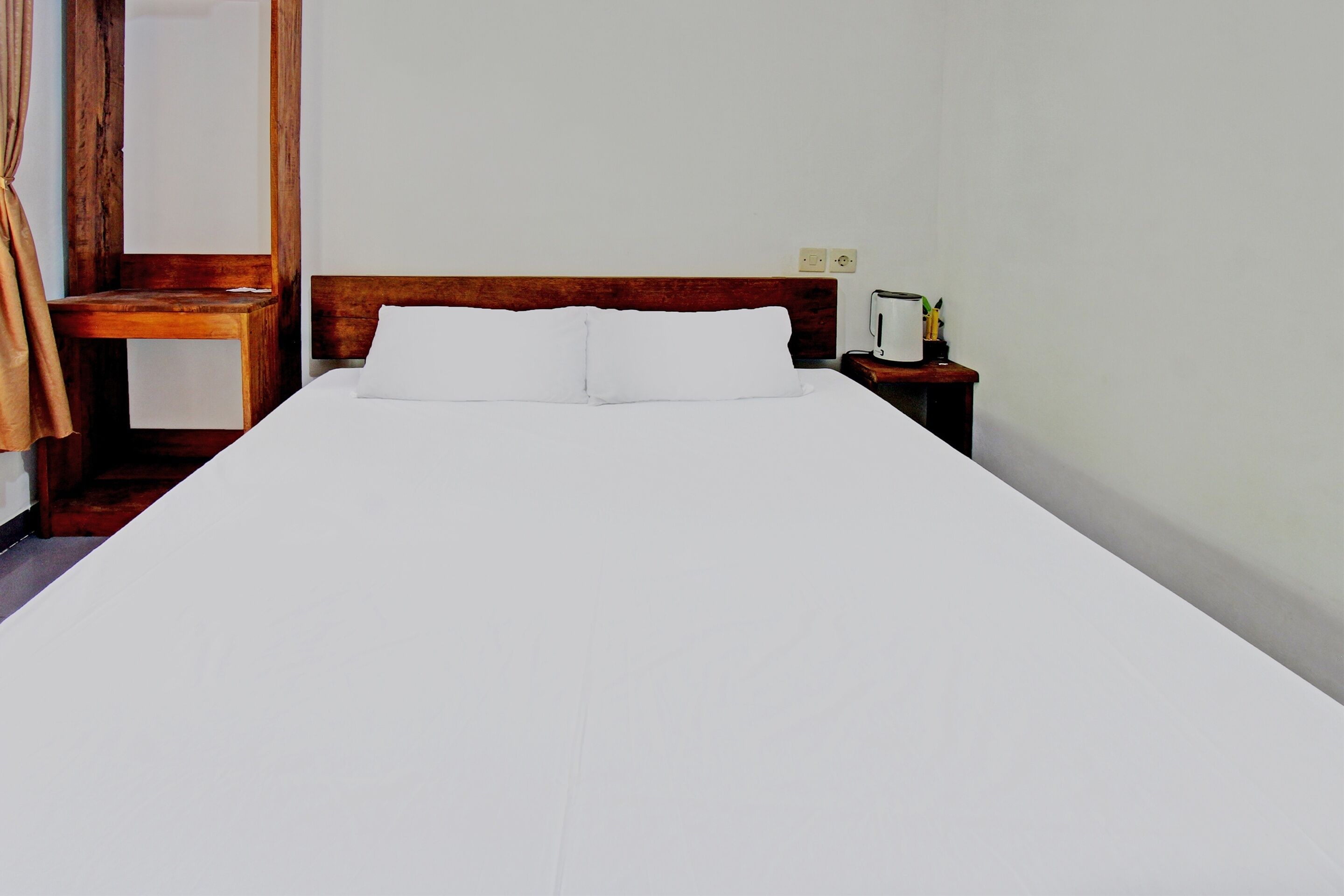 Cama bem arrumada com lençóis brancos em quarto com móveis de madeira e design simples e clean.