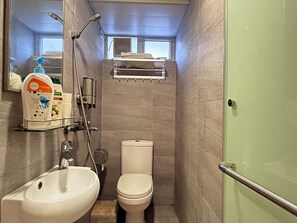 Casa de banho compacta com lavatório, sanita e chuveiro. Produtos de higiene pessoal numa prateleira e porta-toalhas acima da sanita.