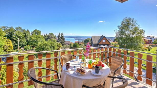Uma varanda com uma mesa posta para dois, com vista para um lago e casas.