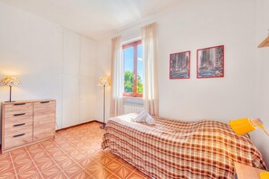 Um quarto com uma cama, cômoda, janela com cortinas e duas fotos emolduradas na parede.