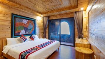 Quarto de cabana de madeira com uma cama grande, uma mesa pequena e vista através de uma porta de vidro.