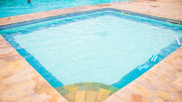 Piscina retangular com borda de azulejos e revestimento de pedra.