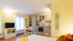 Quarto de hotel compacto com cama, pequena área de refeições, cozinha compacta e televisão.