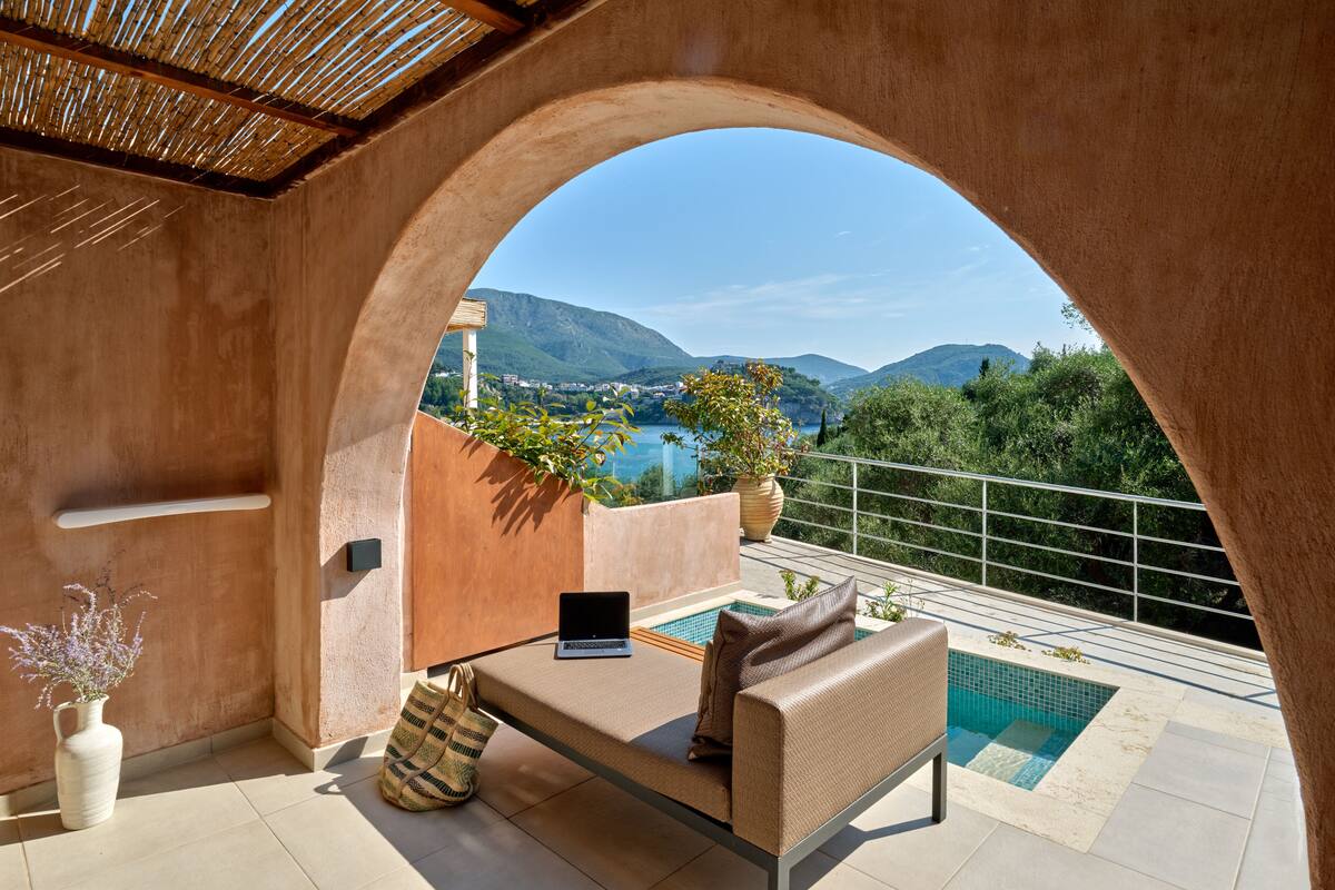Varanda com laptop, sofá e vista para um lago e montanhas.