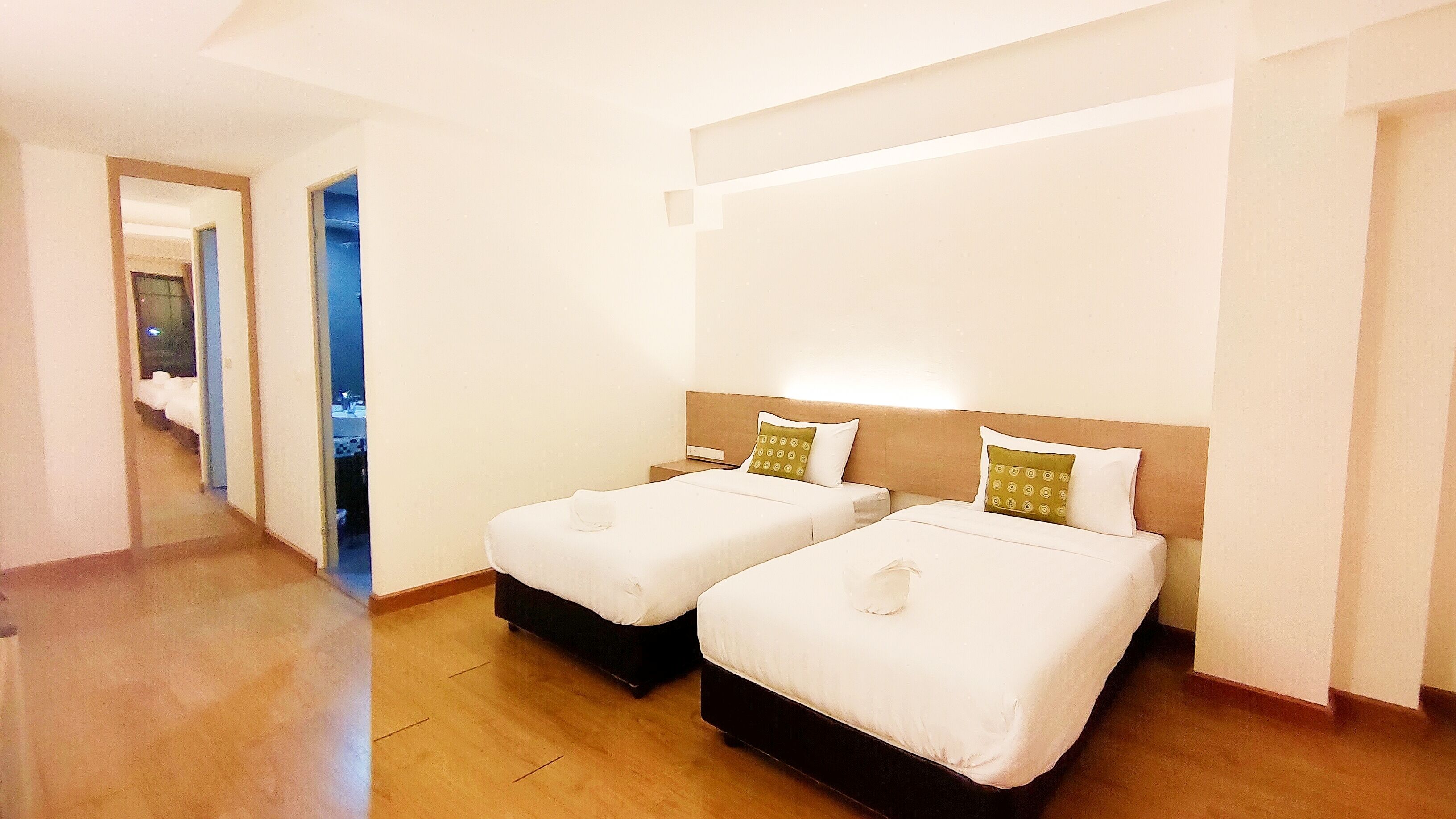 Quarto de hotel com duas camas, chão de madeira e vista da cidade à noite.