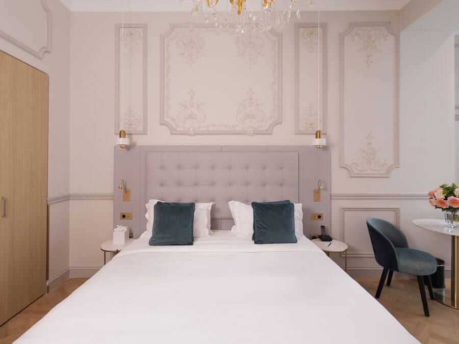Quarto de hotel com uma cama grande, uma mesa redonda com cadeiras e um lustre.