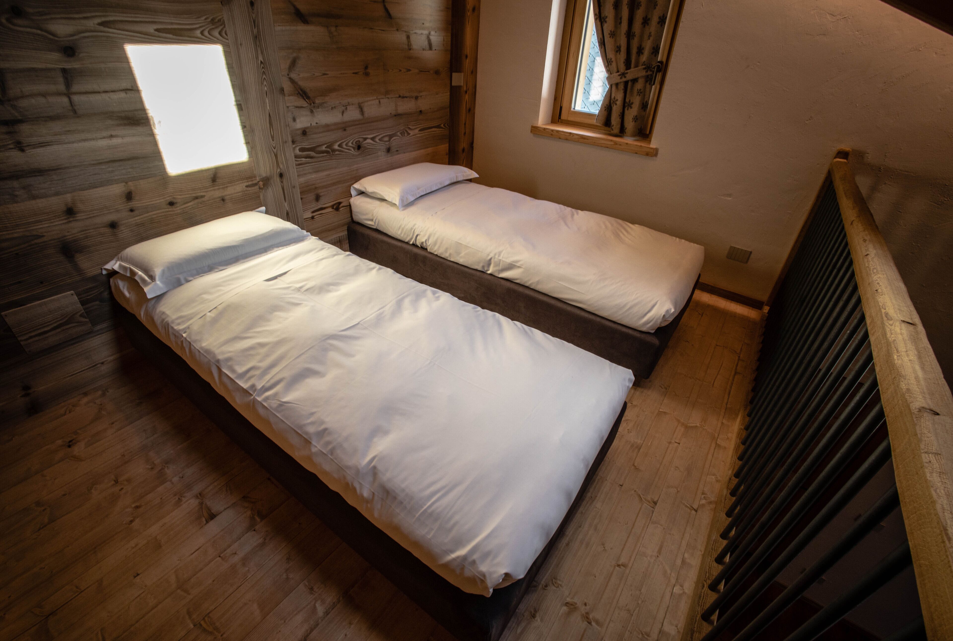 Quarto de cabana de madeira com duas camas simples, uma janela e um radiador.