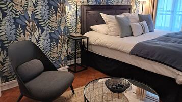 Quarto com cama, cadeira, mesa de centro redonda e parede estampada.