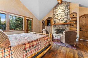 Quarto com uma cama grande, lareira de pedra, estantes de madeira e vista para o exterior.