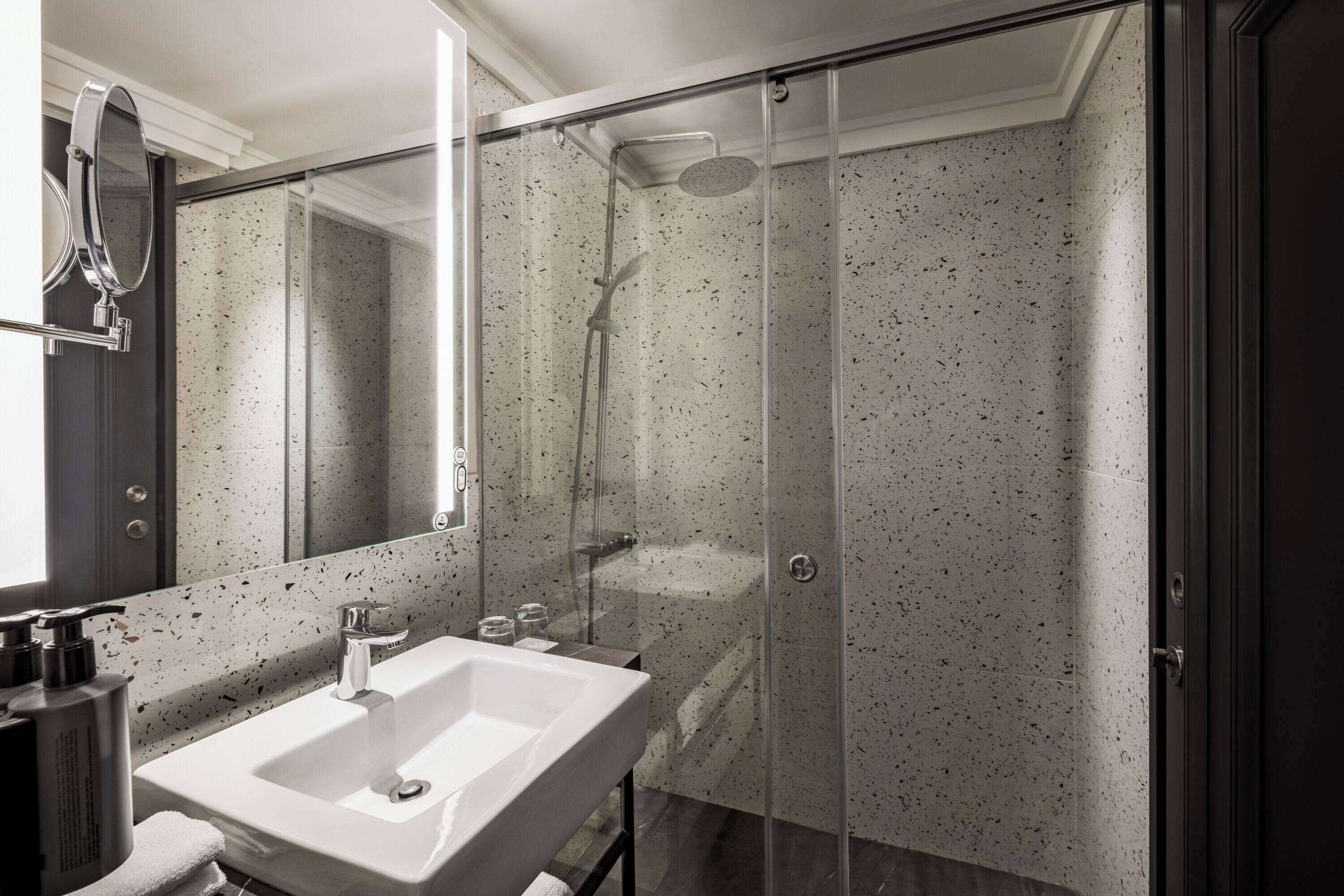 Uma casa de banho moderna com chuveiro envidraçado, lavatório branco e espelho grande.
