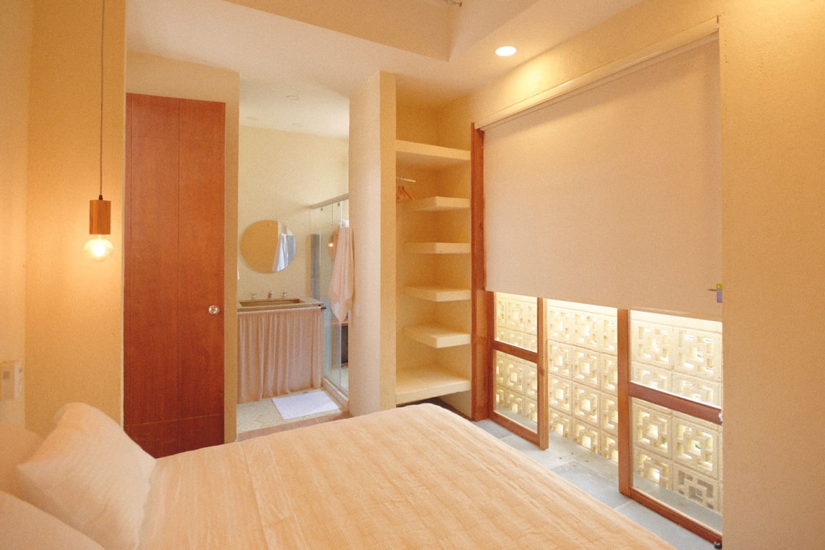 Quarto com cama, porta de madeira, espelho, pia e guarda-roupa.
