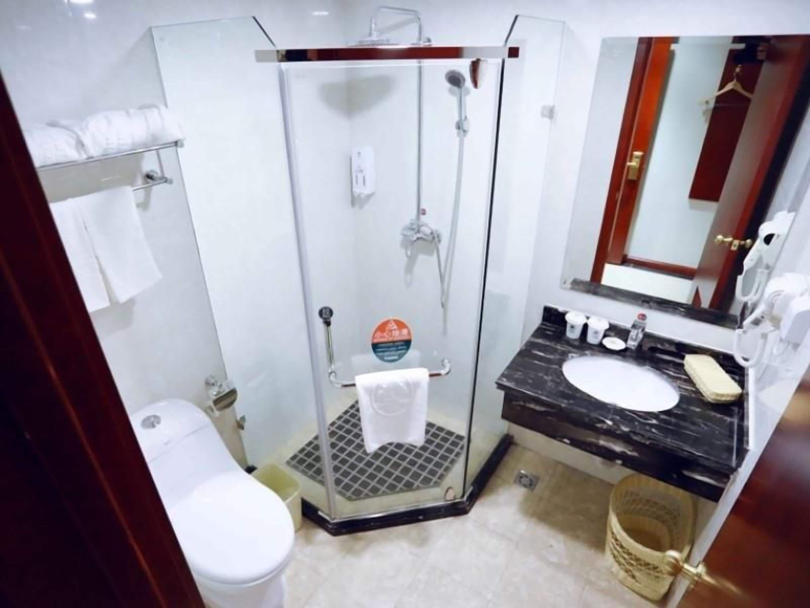 Um banheiro moderno com chuveiro em box de vidro, vaso sanitário branco, pia com bancada preta e espelho sobre a pia.