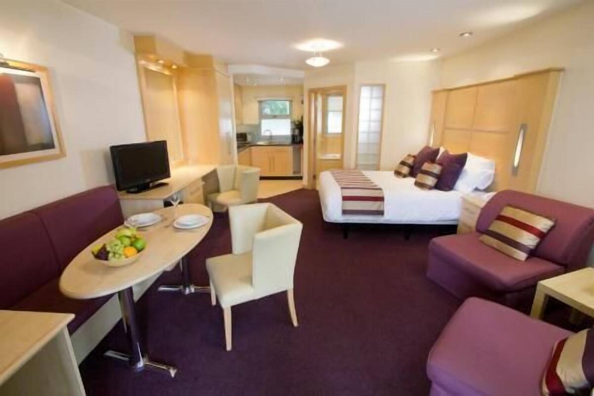 Quarto de hotel com cama, escrivaninha, cadeira, sofá e televisão.