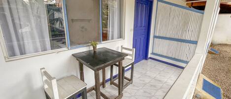 Um quarto pequeno com uma mesa, duas cadeiras, uma janela com cortina e uma porta azul.