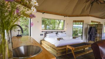 Quarto com cama de madeira, uma mesinha, pia e janela com vista para árvores.