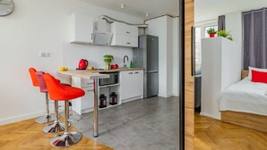 Cozinha compacta com eletrodomésticos modernos, área de jantar com cadeiras vermelhas e quarto com cama e cortinas.