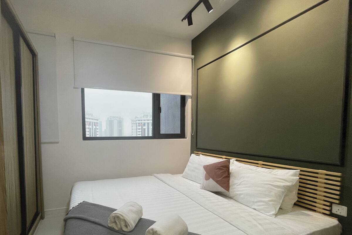Quarto de hotel moderno com uma cama grande, uma janela vista para a cidade, uma mesinha de cabeceira e um painel de cabeceira.