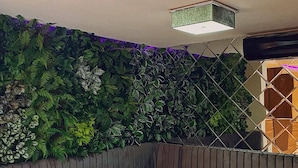 Um espaço de estar no canto com um banco acolchoado, parede com folhagem verde e luminária no teto.