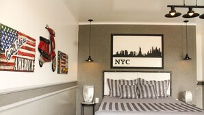 Quarto de hotel com uma cama, um pôster da linha do horizonte da cidade e uma decoração de carro antigo.