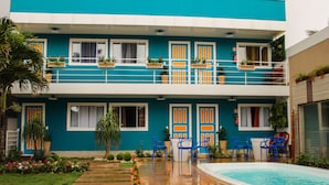 Um edifício de dois andares com piscina, área de estar externa e vasos de plantas.