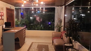 Quarto com balcão de recepção, sofá e uma grande janela com vista para o céu noturno e luzes distantes.