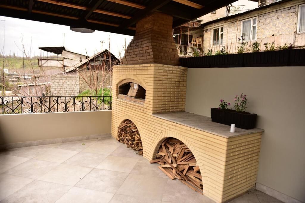 Forno de tijolos ao ar livre com chaminé, pilha de lenha e um vaso com flores.