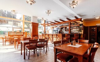 Um restaurante com mobiliário de madeira, espaço de bar e grandes janelas.