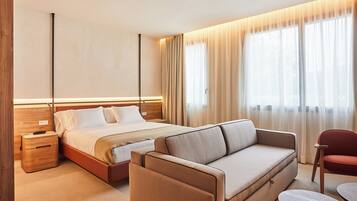 Quarto de hotel moderno com cama, sofá, poltrona e mesa pequena.