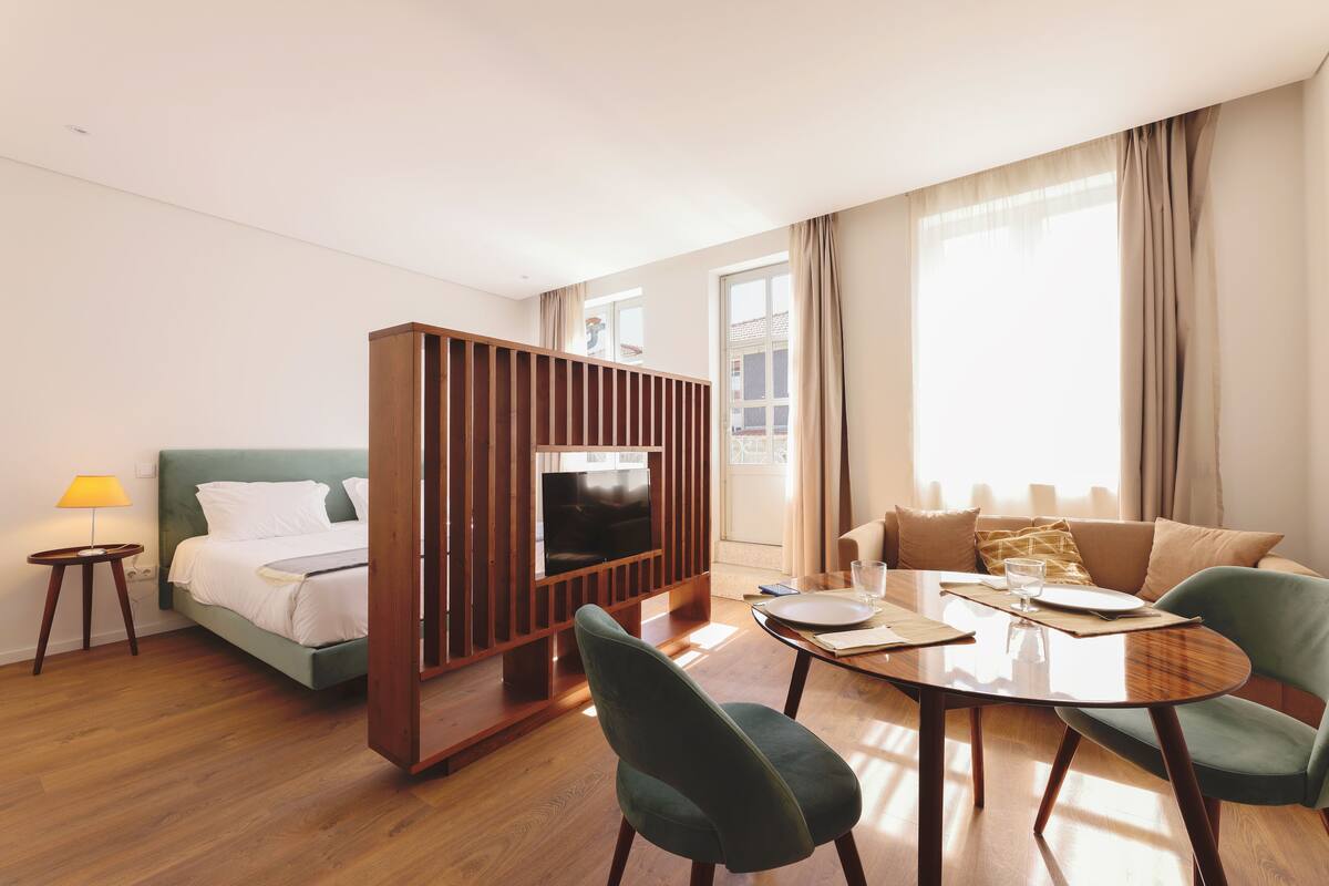 Quarto de hotel com cama, televisão, mesa de jantar com cadeiras e sofá.