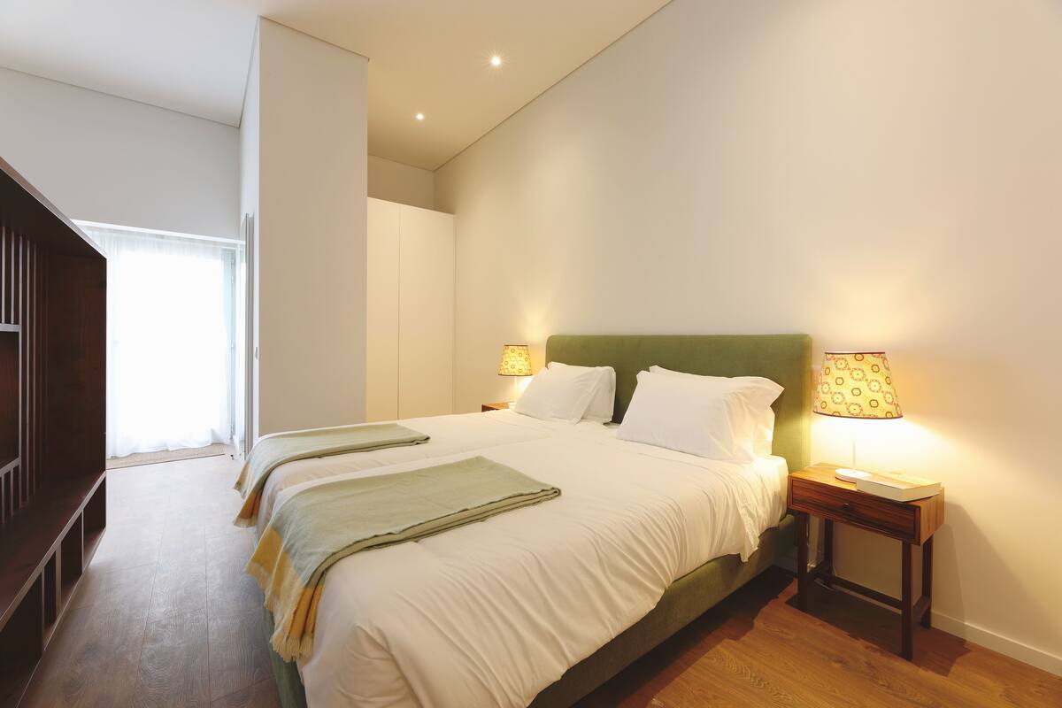 Quarto com uma cama grande, duas luminárias de cabeceira e uma mesinha de cabeceira.