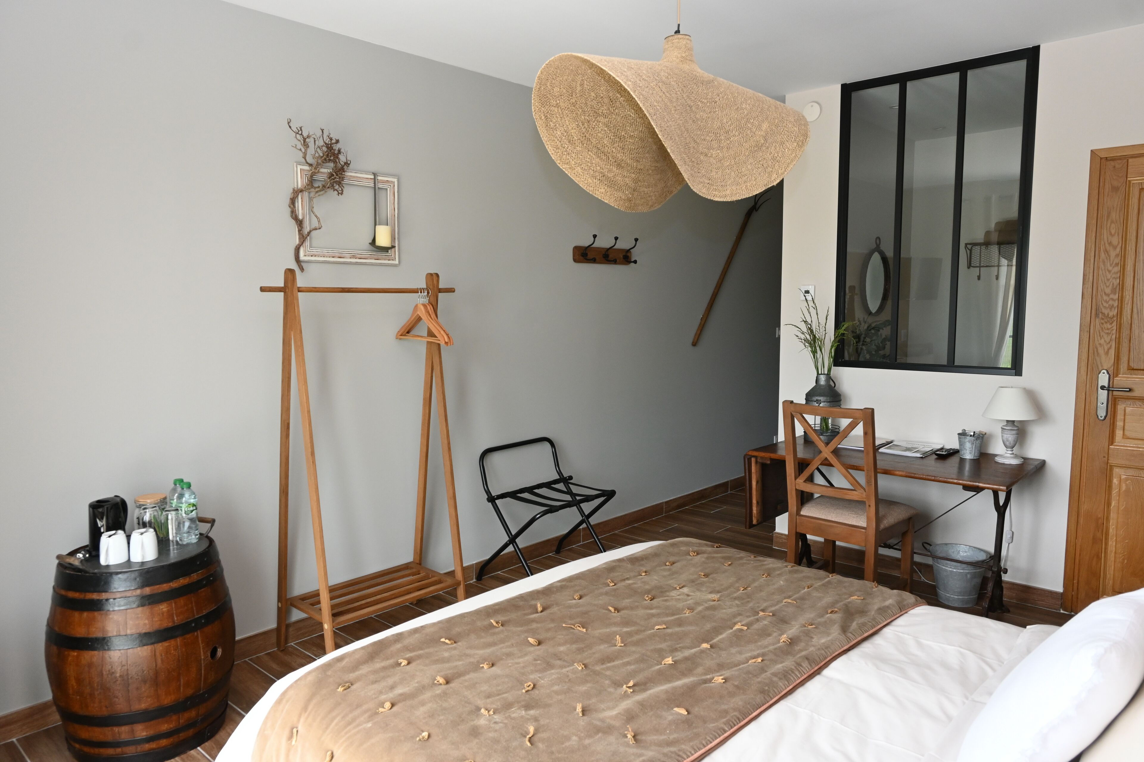 Quarto com cama, escrivaninha, cadeira, luminária pendente e um barril de madeira.